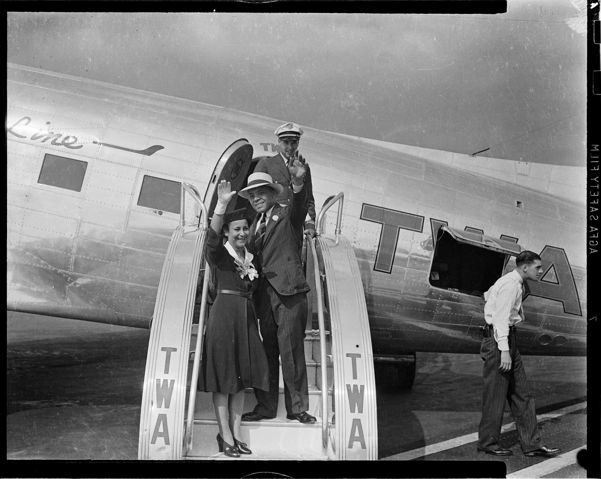 Man and woman waving from steps into TWA airplane, possibly with pilot ...